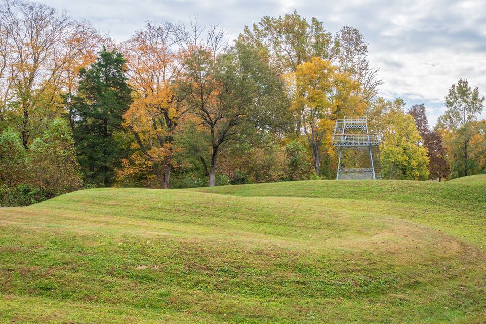 Um parque arborizado com árvores de outono e uma estrutura metálica ao fundo.