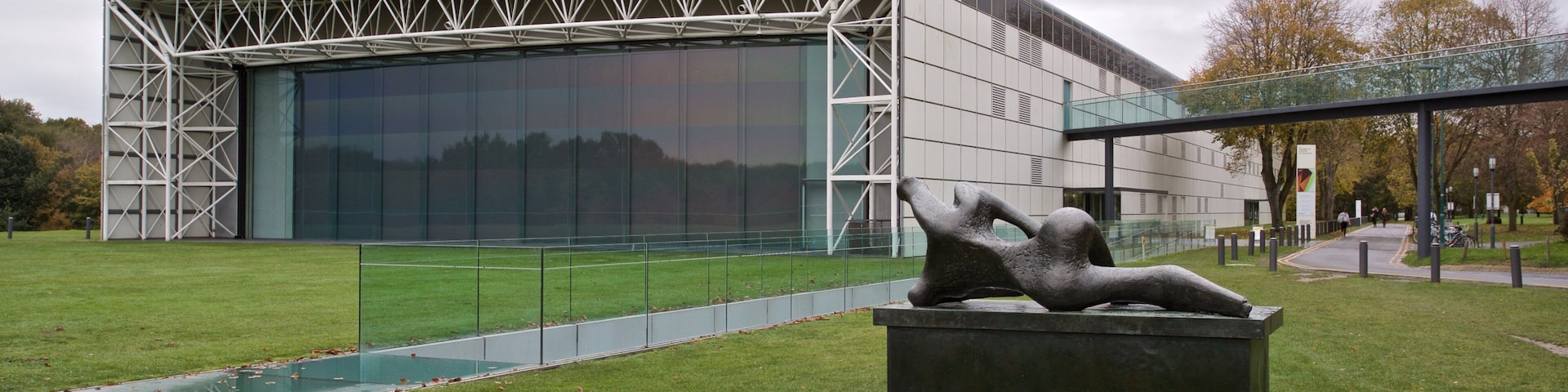 Um edifício moderno com fachada de vidro e uma escultura de uma figura reclinada em um parque.