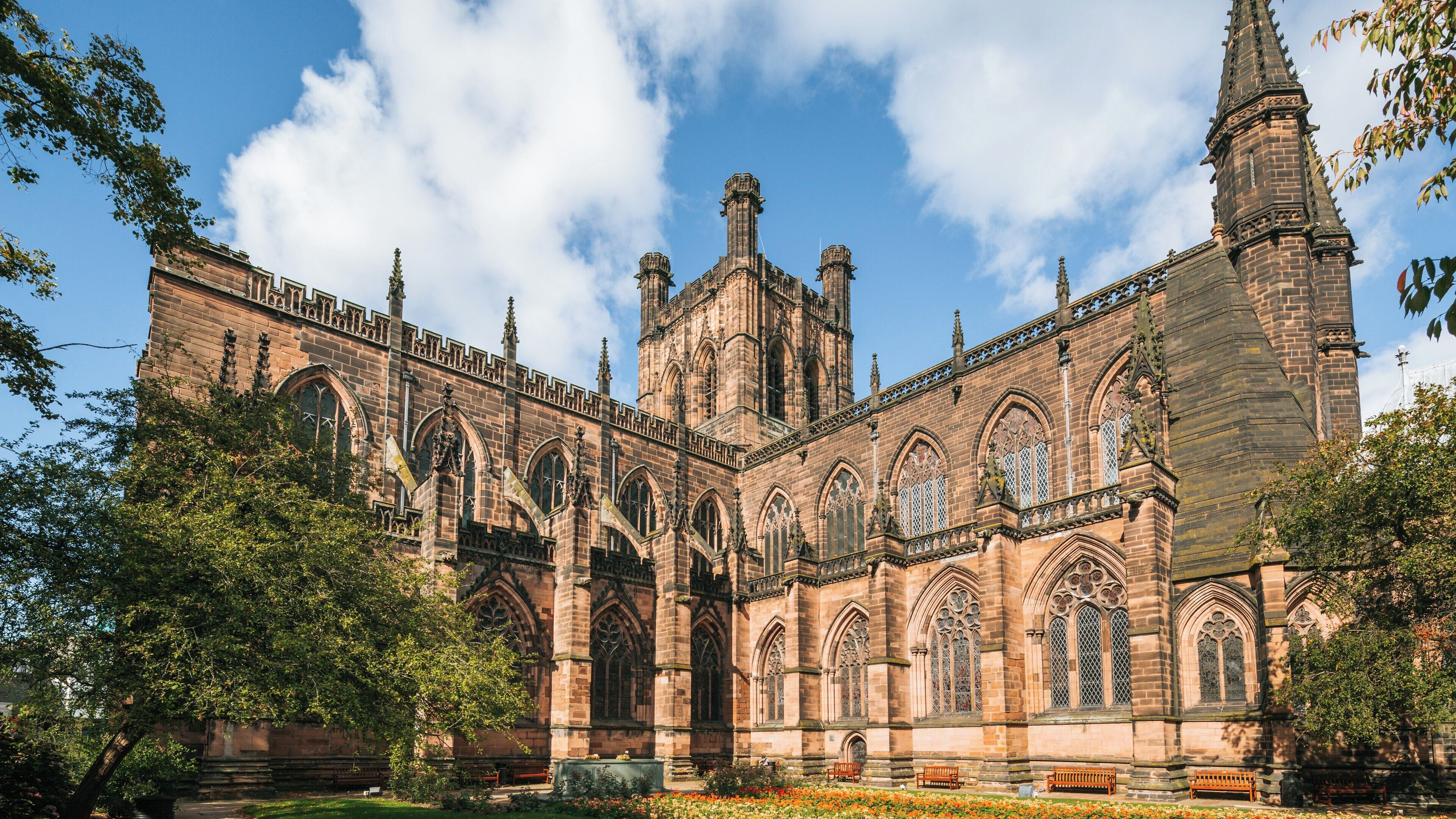 Gothic architecture of Chester Cathedral surrounded by green trees and blue skies in Chester, England, inviting visitors to explore its historical significance and beauty