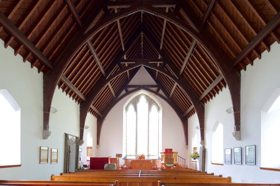 Interior de igreja com bancos de madeira, teto de madeira e amplas janelas em arco.