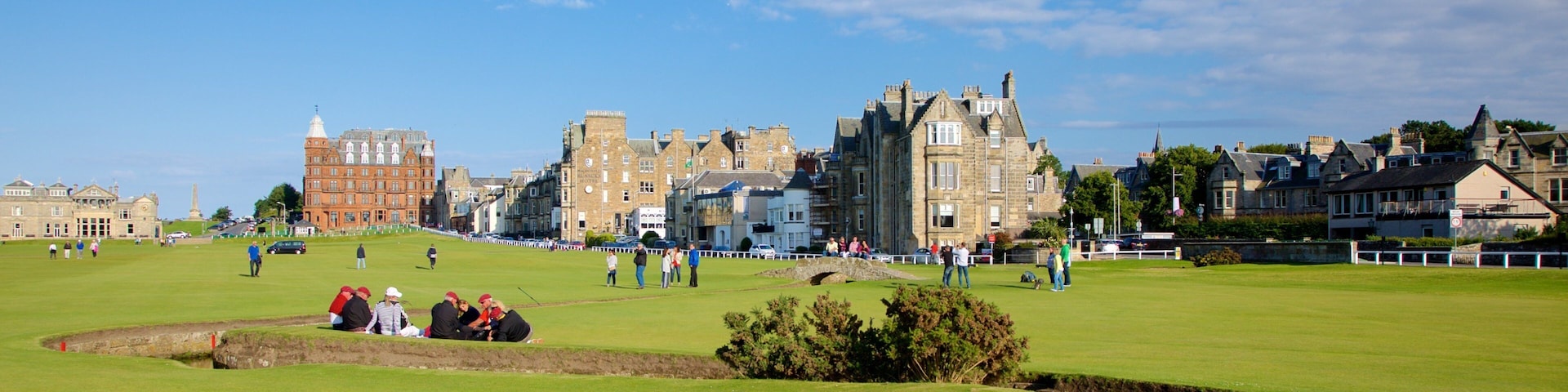 Um campo de golfe com edifícios históricos ao fundo.