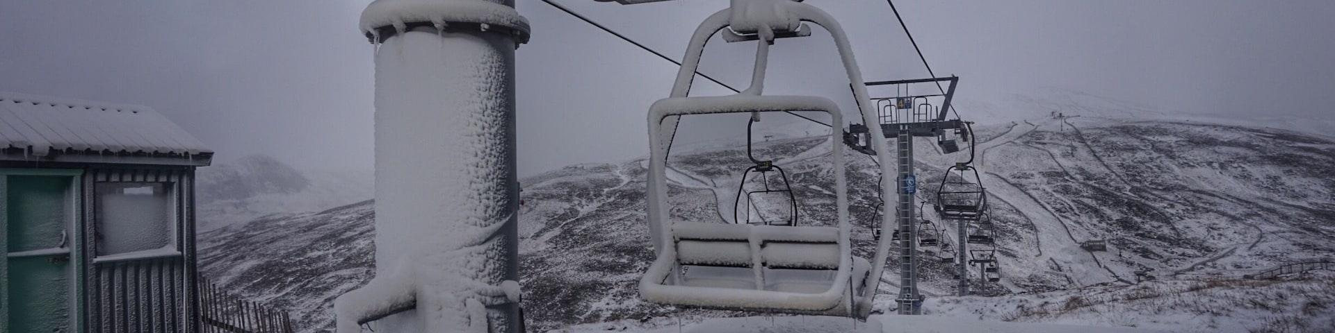 Um teleférico coberto de neve, com uma cadeira em primeiro plano e uma montanha ao fundo.