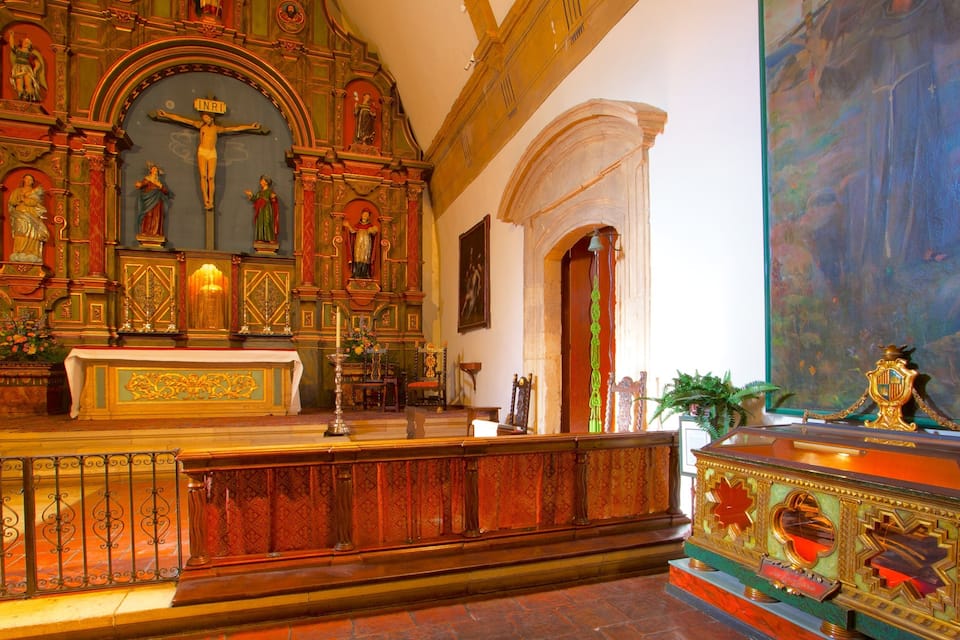 Interior de igreja ornamentado com um crucifixos, altar e pinturas religiosas.