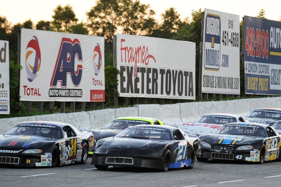 Uma pista de corrida com vários carros de corrida e outdoors publicitários.