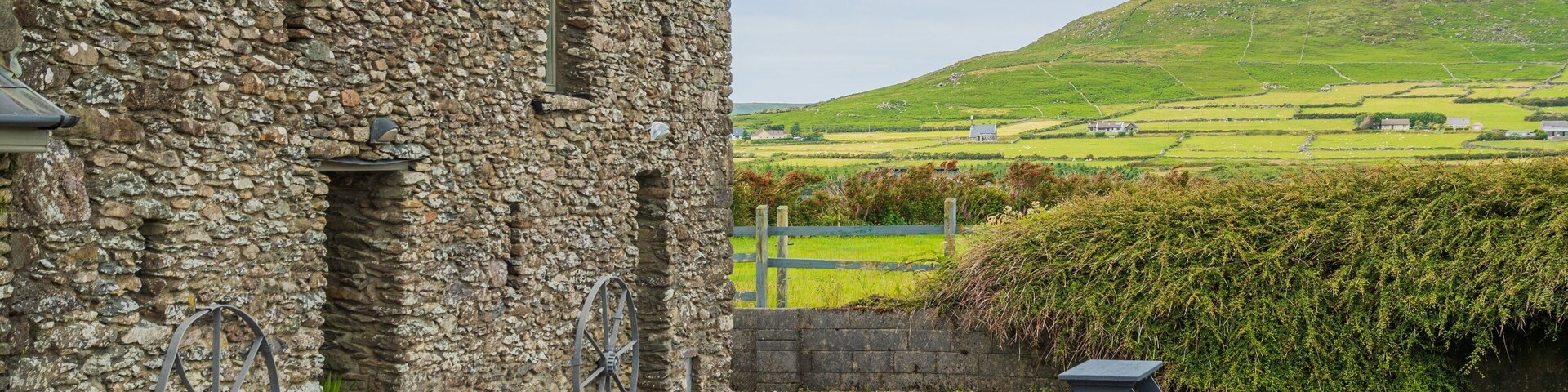 Um edifício de pedra com uma bicicleta, mesas de piquenique e uma paisagem verde ao fundo.