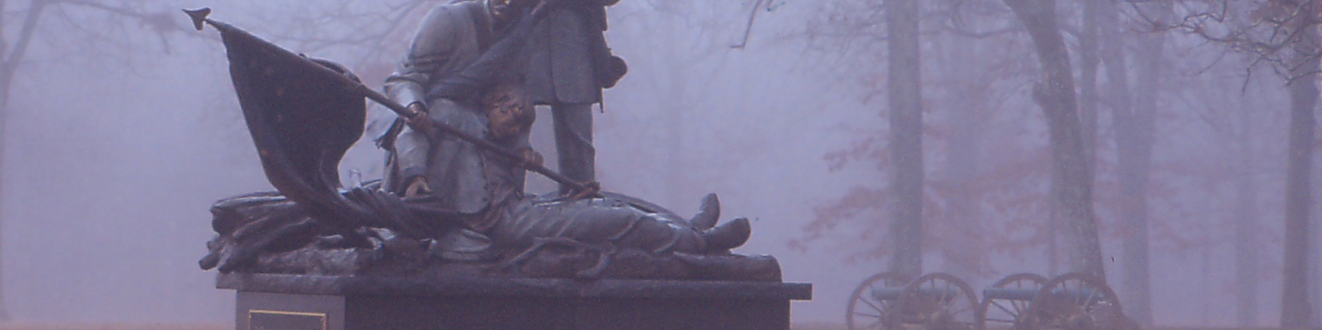 A statue of a soldier on horseback with a fallen comrade, labeled "TENNESSEE," in a foggy setting with bare trees and a cannon in the background.