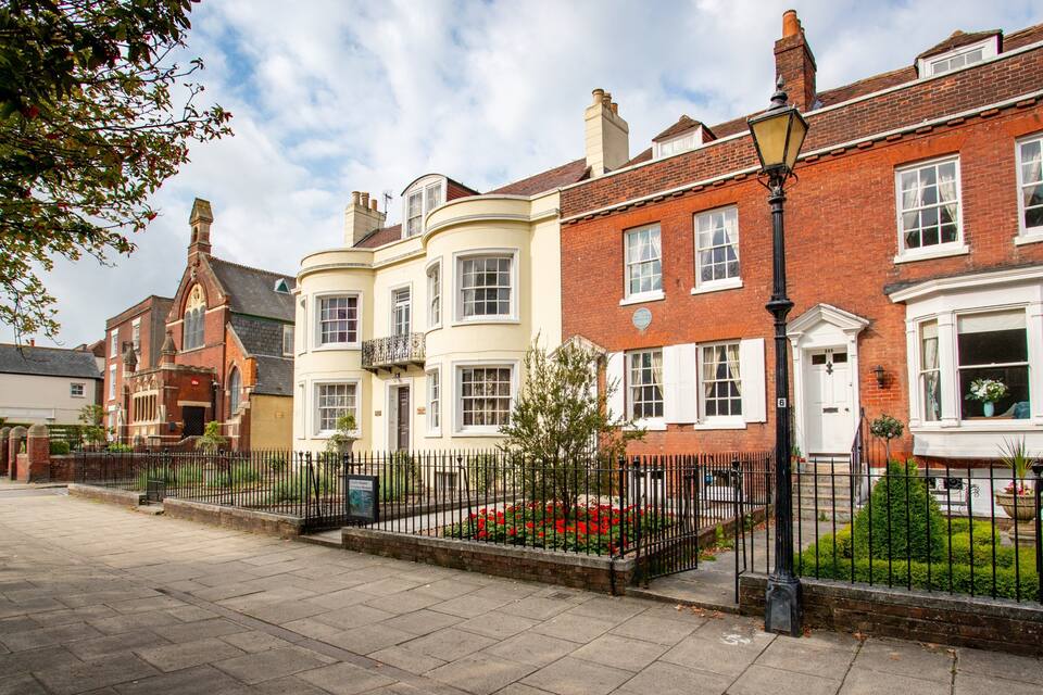 Fileira de casas geminadas britânicas tradicionais, com cerca de metal preta e flores vermelhas no jardim da frente.