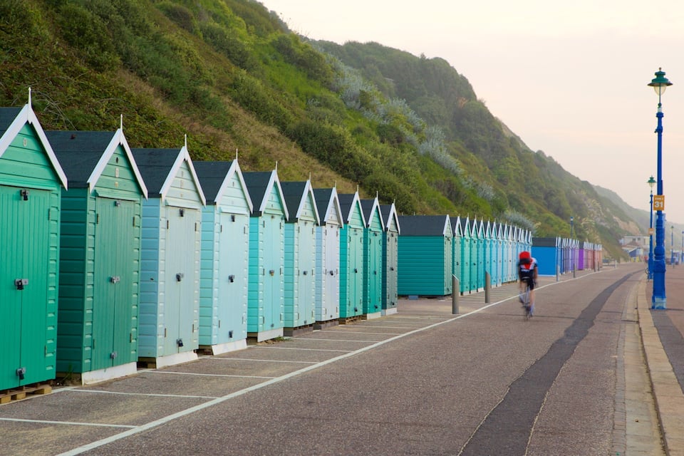 Uma fileira de cabanas de praia ao longo de um calçadão à beira-mar, com um ciclista ao longe.