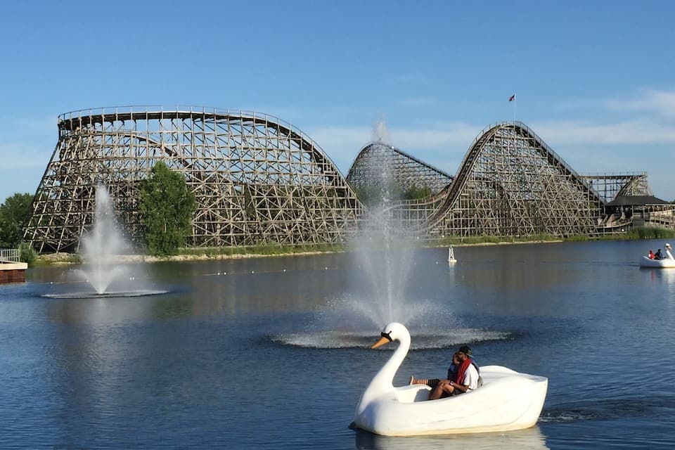 Um barco em forma de cisne em um lago, com montanhas-russas ao fundo.