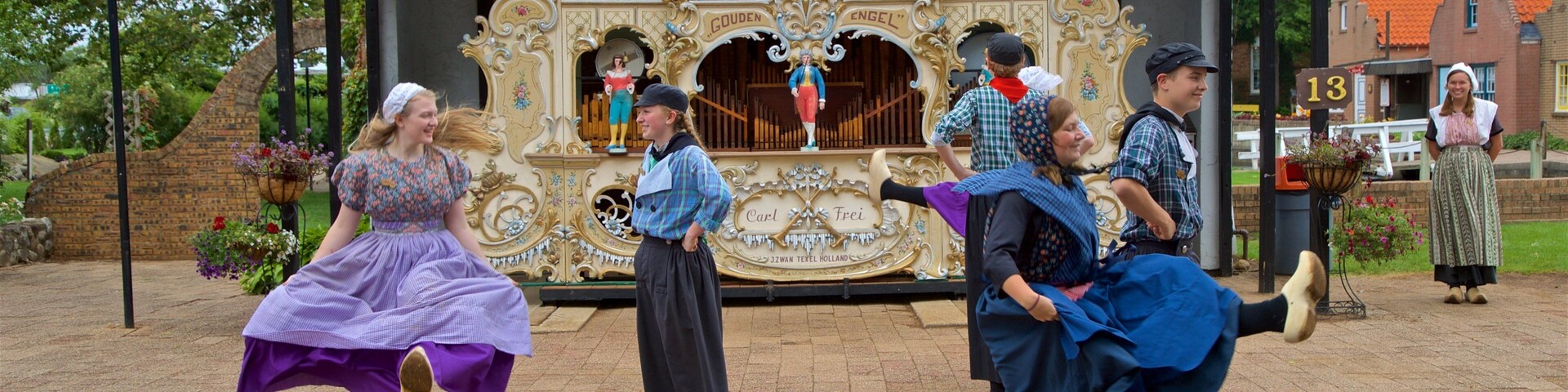 Apresentação de dança tradicional holandesa em frente a uma igreja com decorações elaboradas e uma placa com o dizer 'DANSPEIN'.