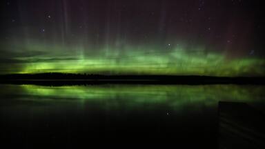 Aurora Boreal refletida sobre um lago calmo à noite.