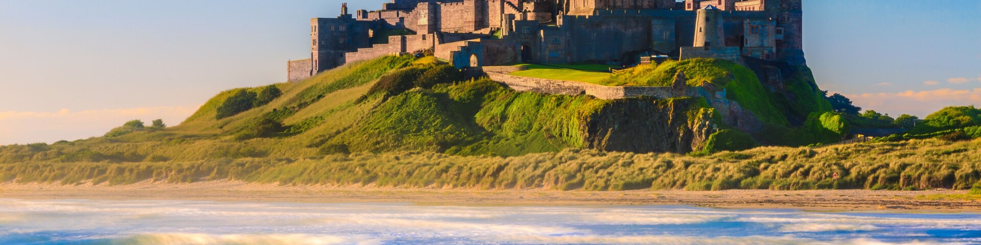 Um castelo histórico numa colina com vista para o oceano.