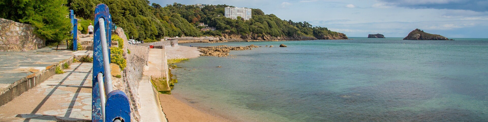 Um passeio à beira-mar com vista para o oceano, uma praia de areia e um edifício numa colina.
