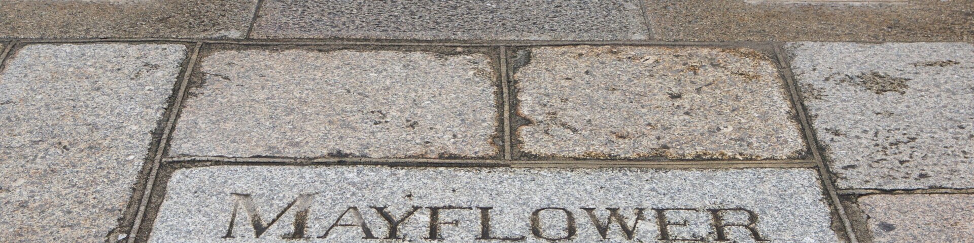 Uma placa de pedra com a inscrição 'MAYFLOWER 1620' em um caminho pavimentado.