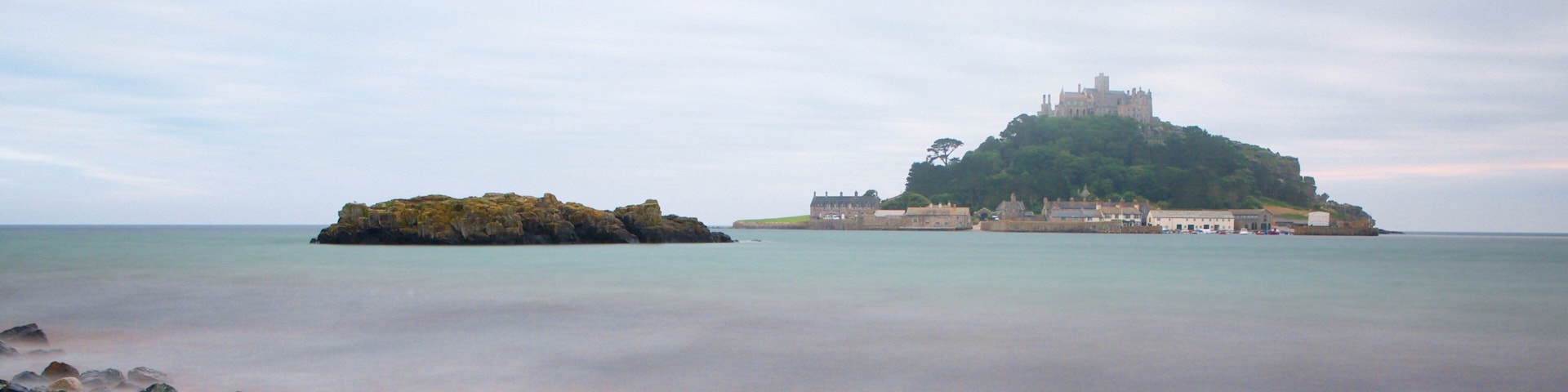 Um castelo numa colina com vista para um mar calmo, rodeado por costas rochosas.