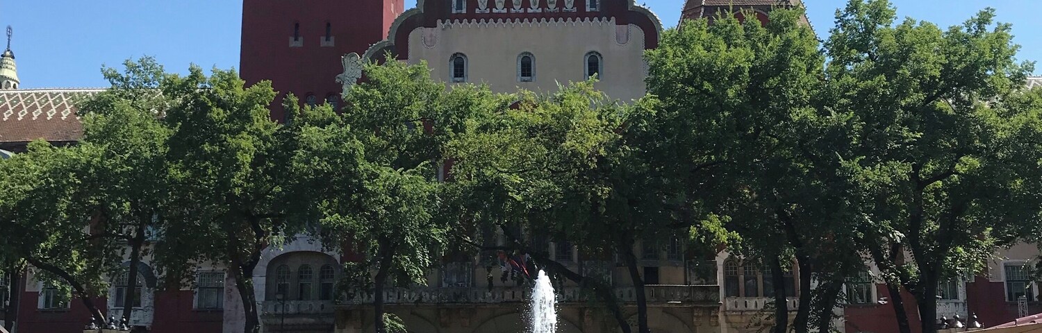 Um edifício histórico com uma torre do relógio, uma fonte e uma torre vermelha.