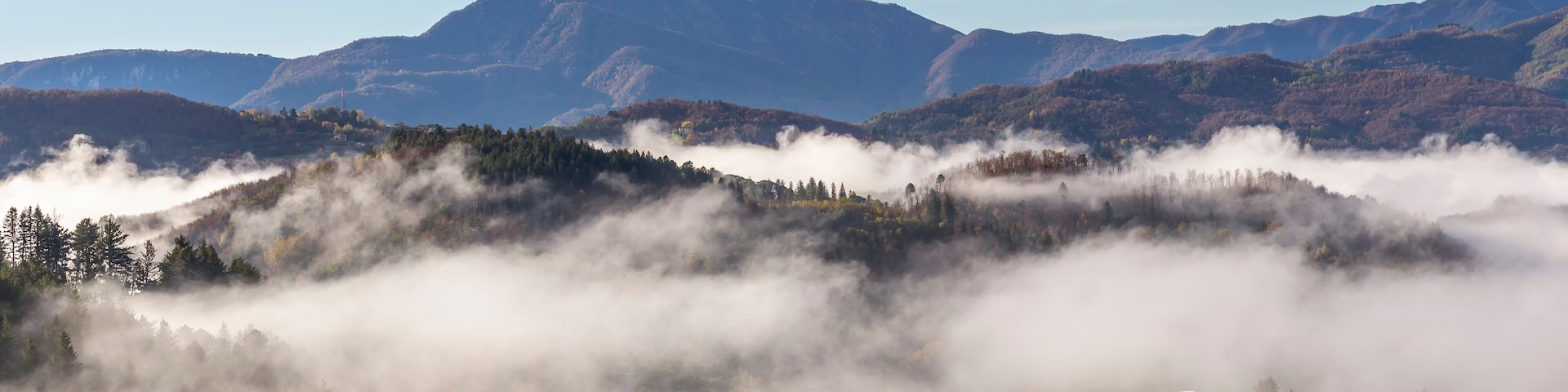 Paisagem montanhosa com florestas densas e picos cobertos de névoa.
