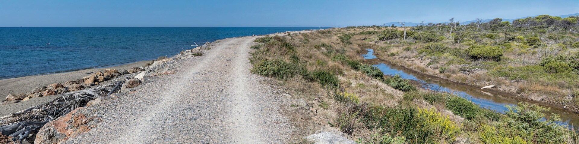 Uma estrada de cascalho que leva a uma praia, com um pequeno riacho à direita.