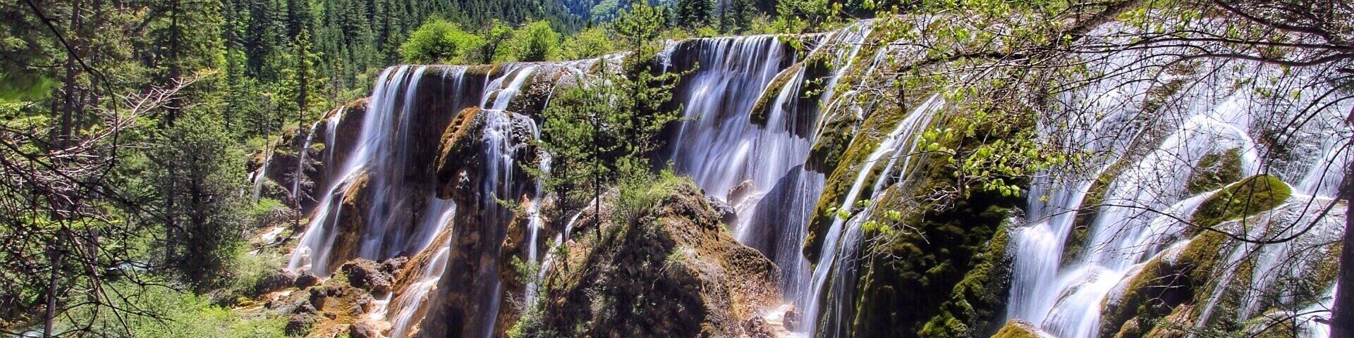 Uma cascata com vários níveis, rodeada por vegetação exuberante e montanhas.