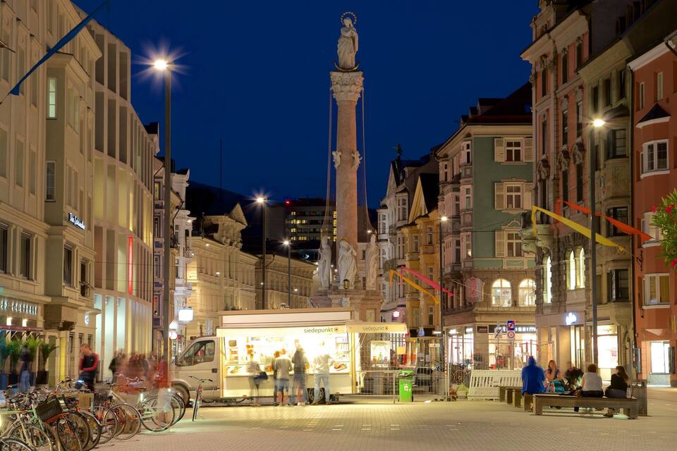 Uma praça urbana com um monumento, postes de luz e edifícios.
