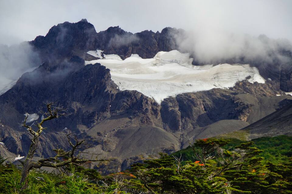 Uma geleira cercada por montanhas acidentadas e vegetação densa.