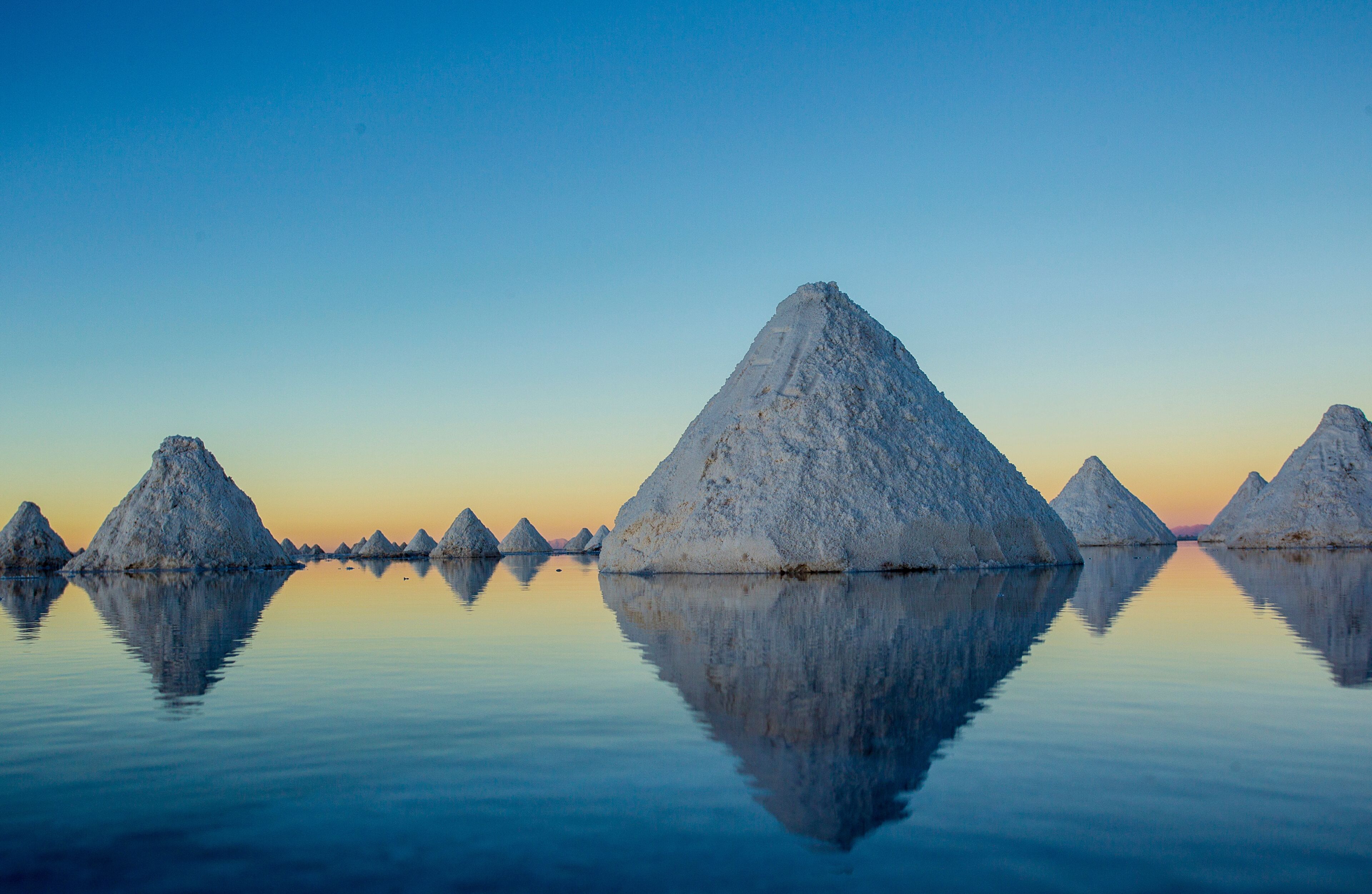 Diversas estruturas piramidais cobertas de neve refletidas em águas calmas, sob um céu claro.