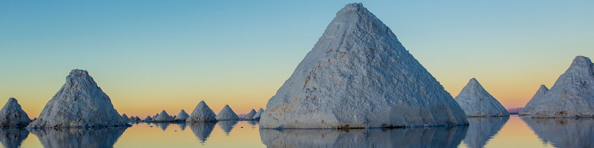 Diversas estruturas piramidais cobertas de neve refletidas em águas calmas, sob um céu claro.