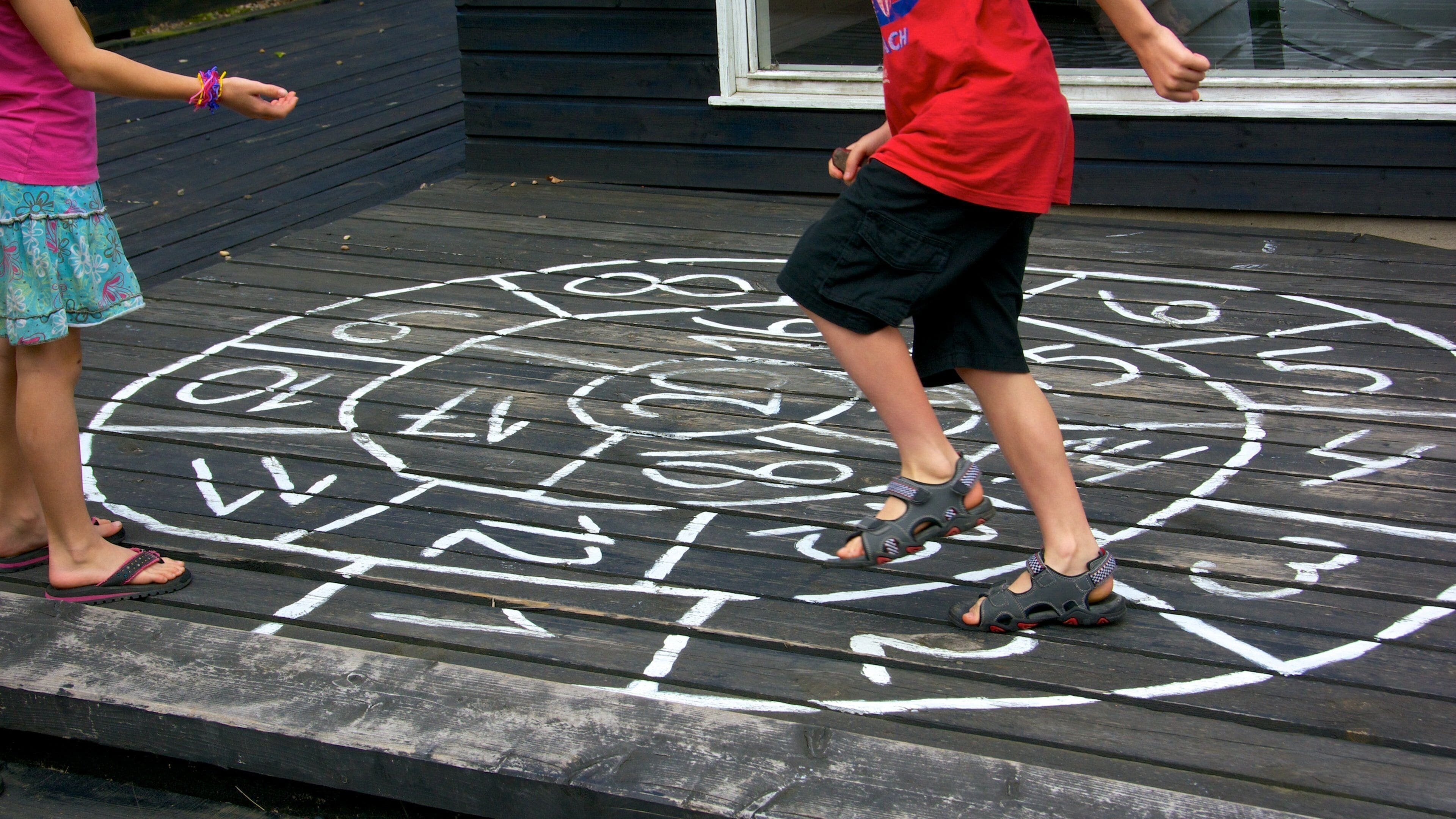 Crianças brincando de amarelinha em um deck de madeira.