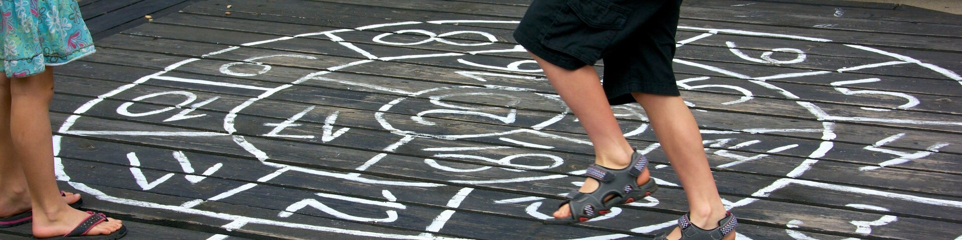 Crianças brincando de amarelinha em um deck de madeira.