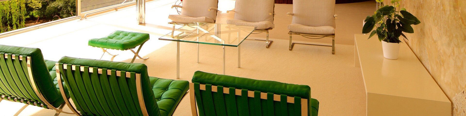 Uma sala de estar moderna com cadeiras verdes, uma mesa de centro de vidro e vista para uma varanda com guarda-corpo.