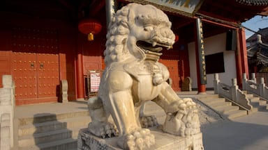Uma estátua de leão de pedra na entrada de um edifício tradicional chinês, com portas vermelhas e telhado telhado.