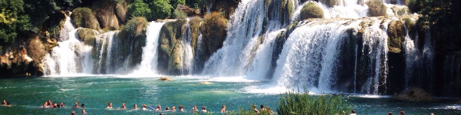 Uma cascata deságua numa piscina azul cristalina, rodeada por vegetação exuberante.