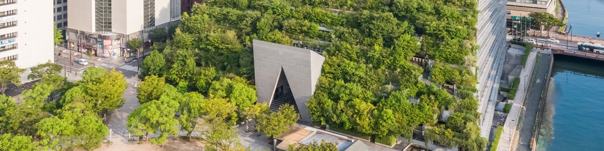 Paisagem urbana com um edifício de destaque e design triangular singular, cercado por vegetação exuberante.