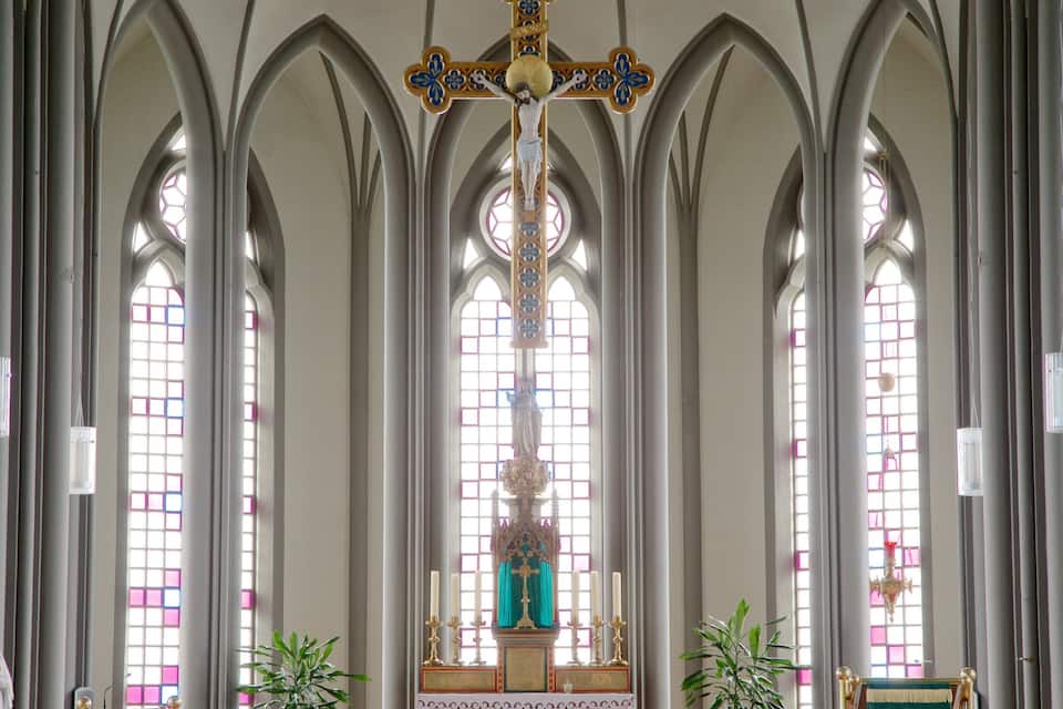 Interior de igreja com crucifixos, vitrais e altar central.