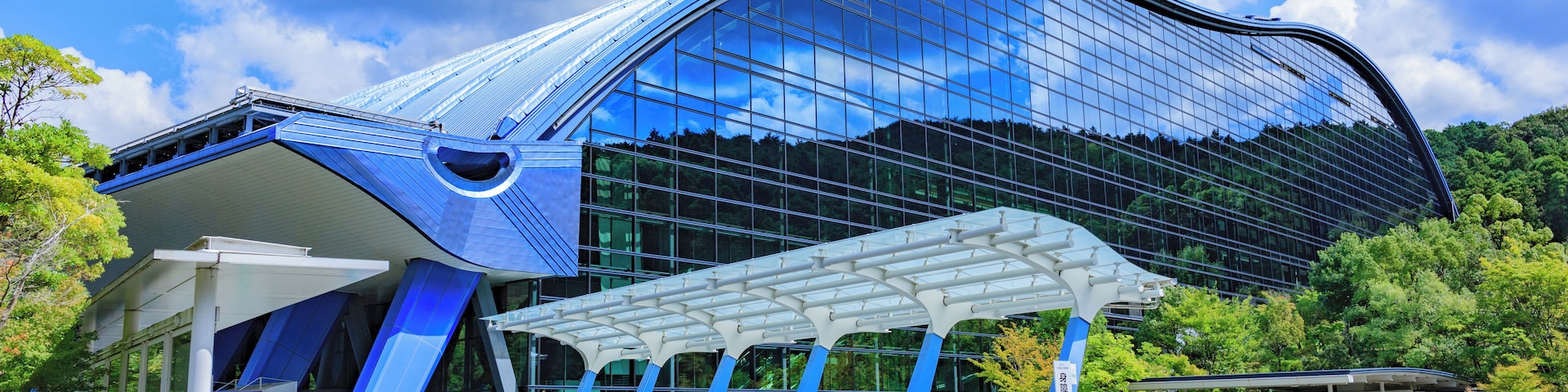 Um edifício moderno de vidro com telhado curvo e detalhes azuis.