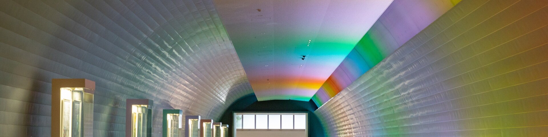 Um espaço interior moderno e bem iluminado, com teto curvo exibindo um espectro de cores do arco-íris.