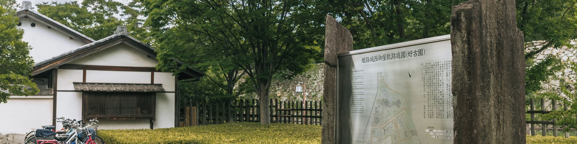 Um edifício japonês tradicional, um monumento de pedra com um mapa e bicicletas estacionadas perto.