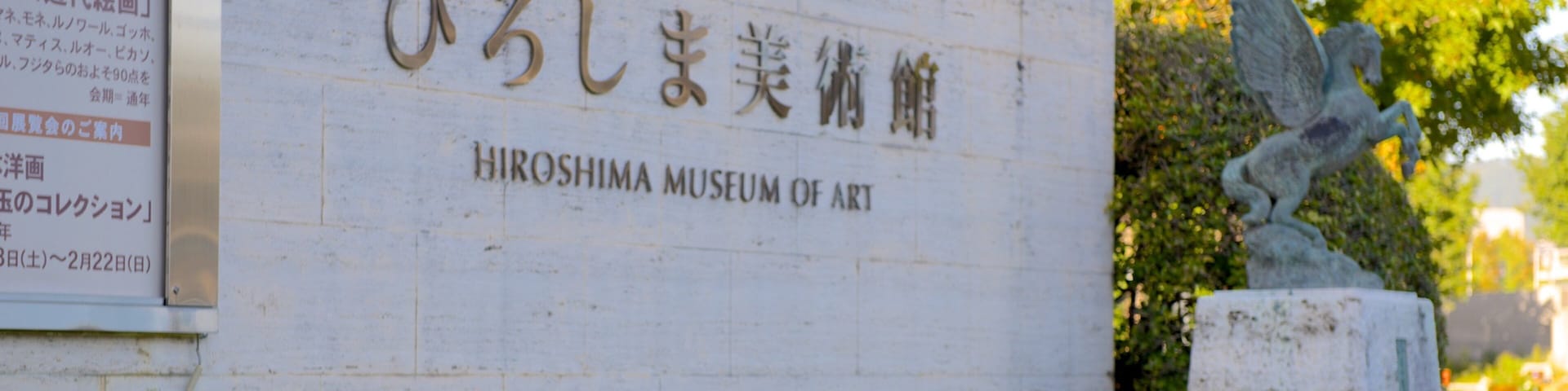 Placa do Museu de Arte de Hiroshima com uma estátua de anjo e flores em primeiro plano.