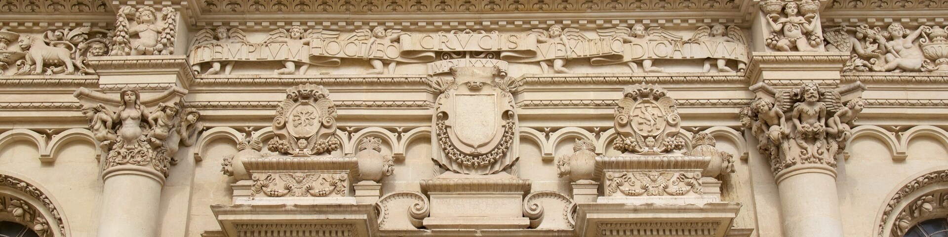 Fachada de edifício com esculturas detalhadas, incluindo leões, querubins e escudos ornamentados.