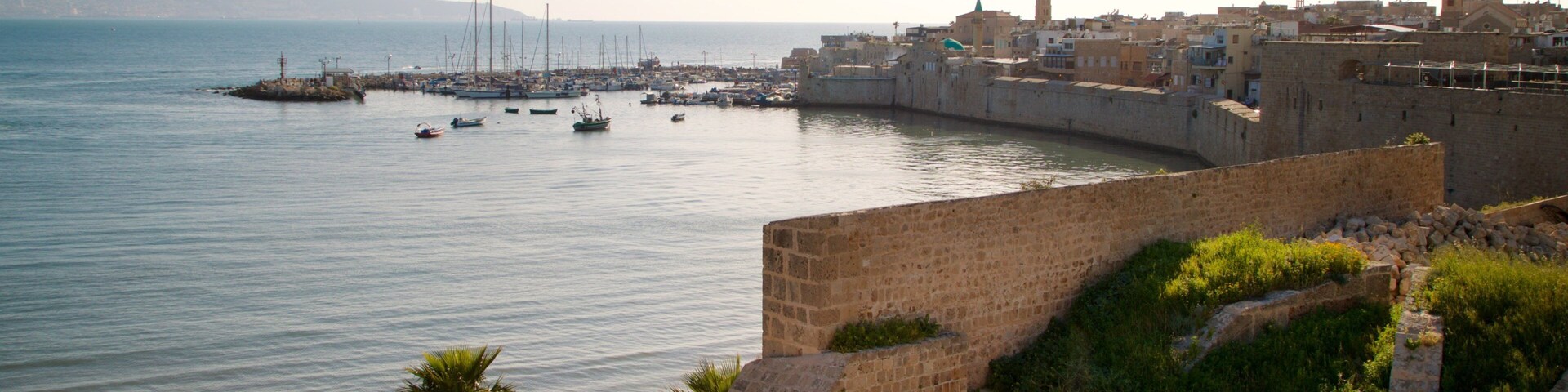 Uma cidade costeira com uma fortificação histórica, mar calmo e barcos.