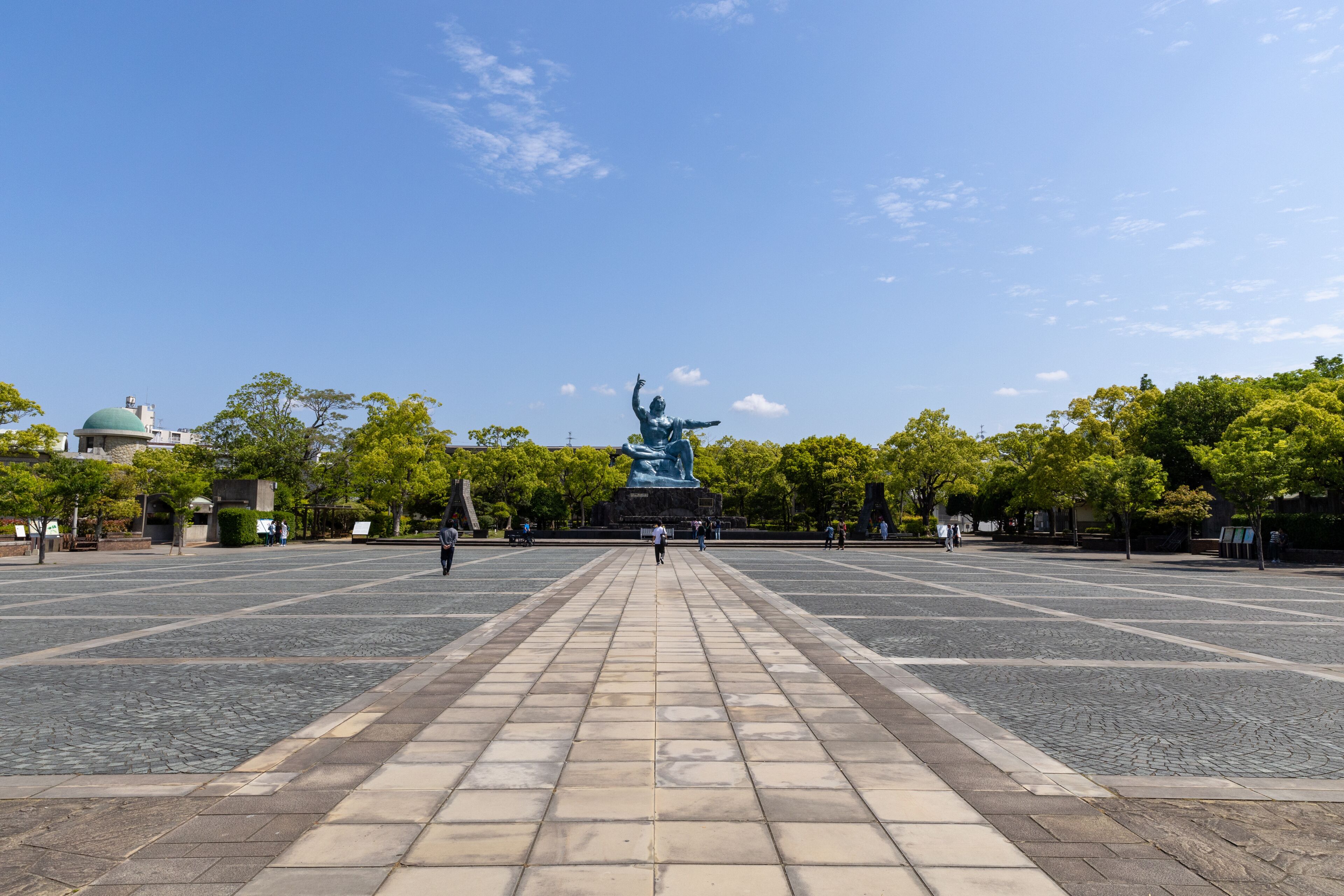 Uma praça ampla com uma estátua central, cercada por árvores e edifícios.