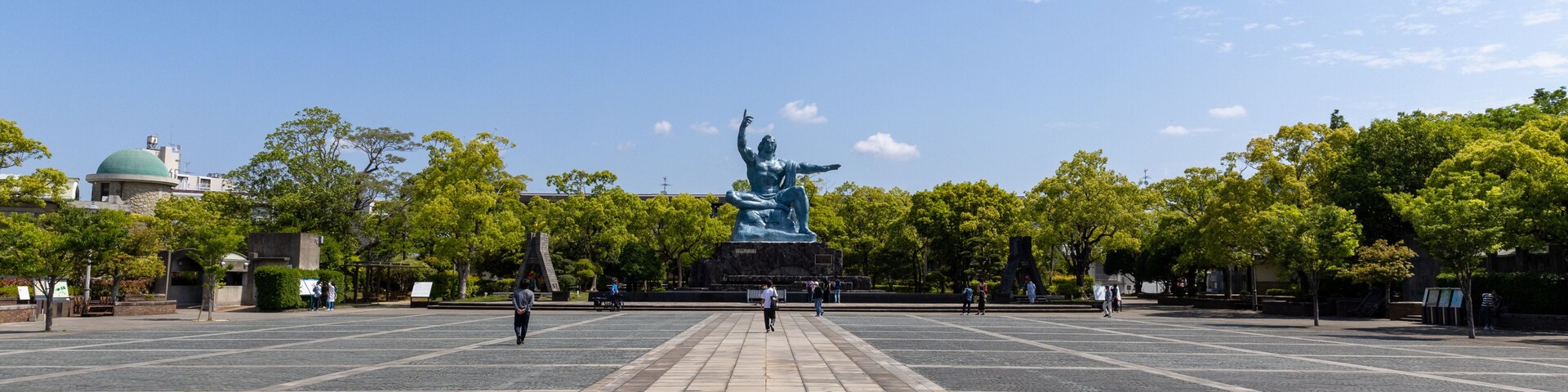 Uma praça ampla com uma estátua central, cercada por árvores e edifícios.