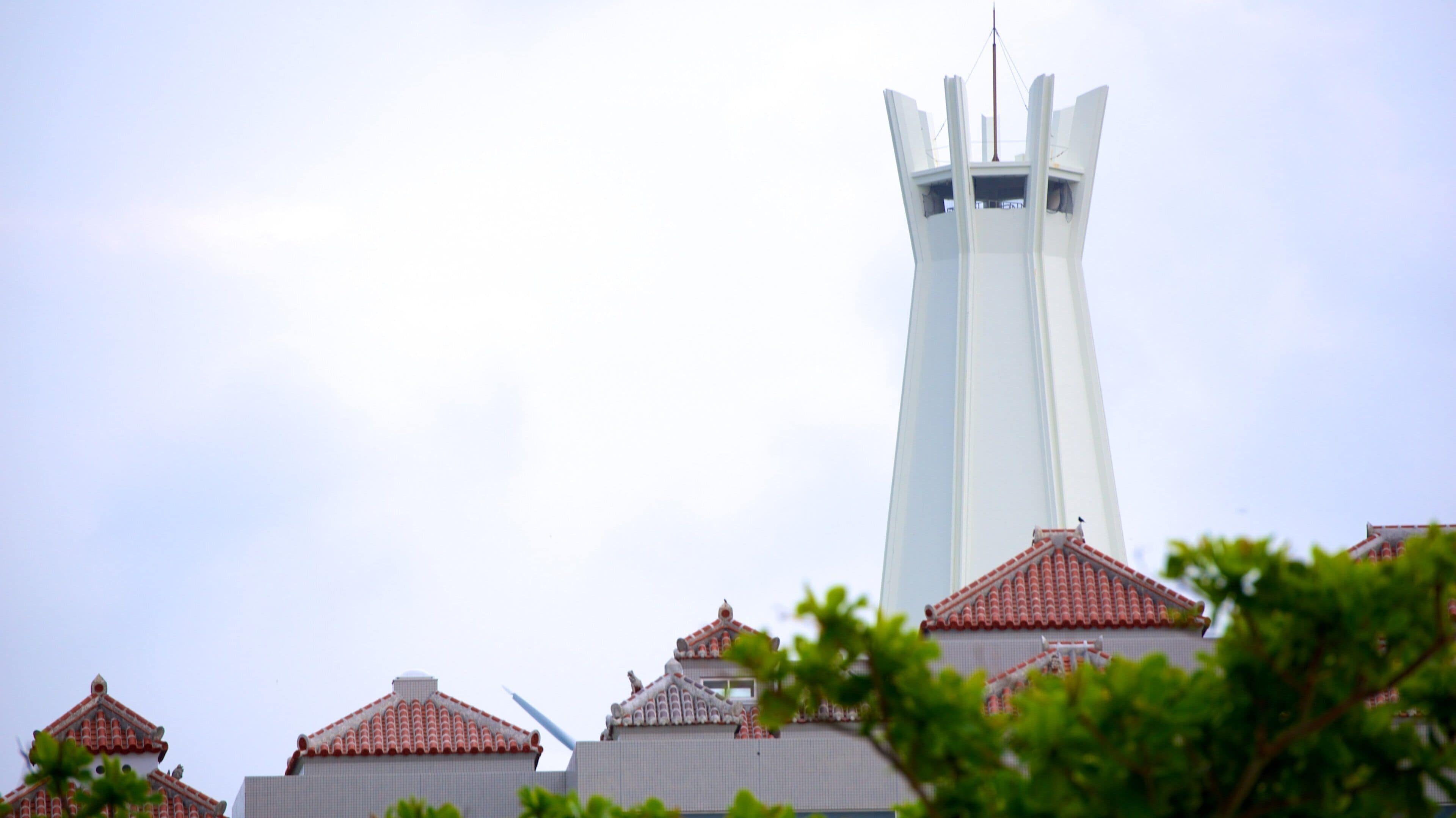 Uma torre com fachada branca e telhado de telhas vermelhas, cercada por edifícios tradicionais com arquitetura semelhante.