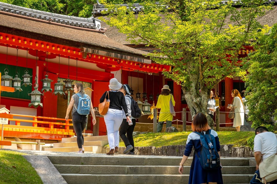 Um templo japonês tradicional com paredes vermelhas e brancas, telhado de telhas e escadaria de pedra que leva à entrada.