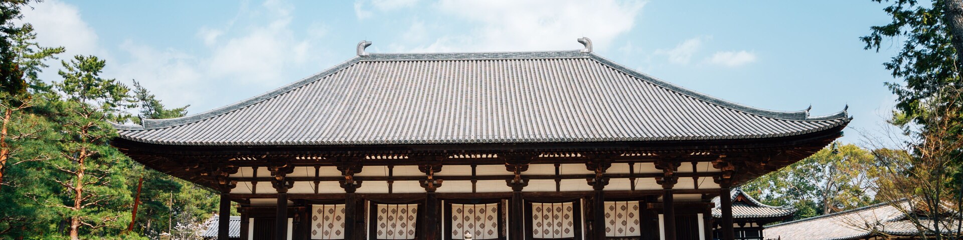Um edifício tradicional japonês com telhado telhado e colunas de madeira, rodeado por um pátio de cascalho e árvores.