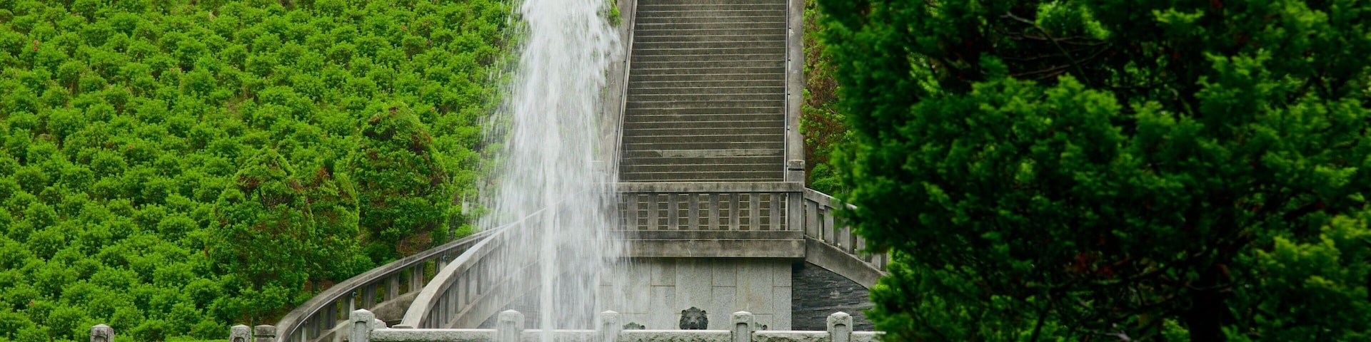 Uma ponte de pedra japonesa tradicional com uma cascata, rodeada por vegetação exuberante.