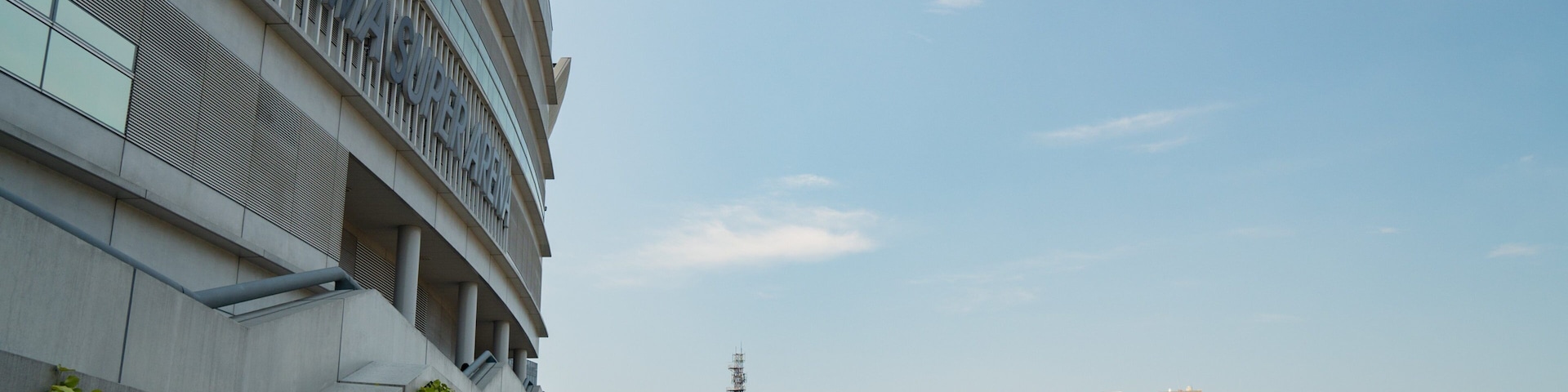 Um edifício moderno com fachada curva e uma passarela para pedestres com áreas verdes.