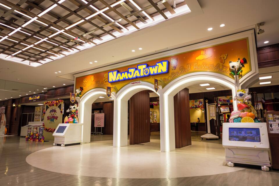 Um espaço interno bem iluminado com um letreiro 'NamJatown', pilares de madeira e várias decorações, incluindo uma estátua de panda.