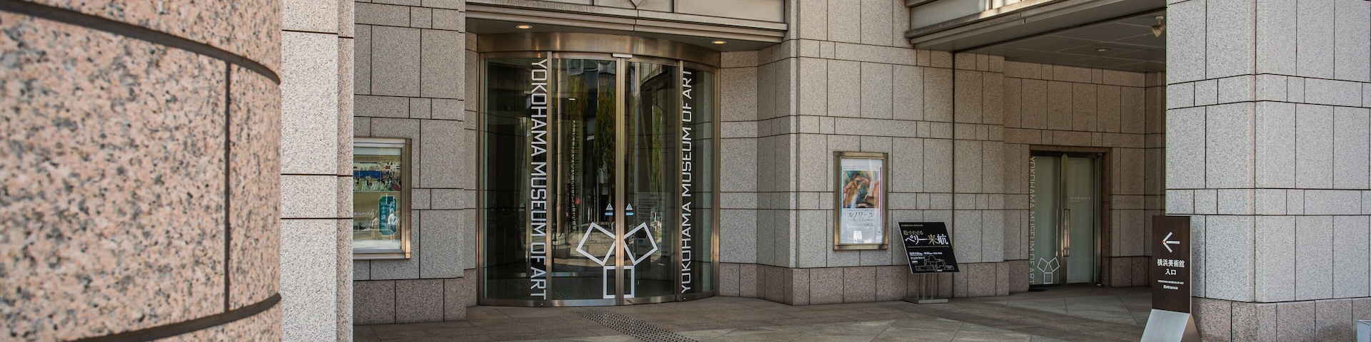 A entrada do Museu de Arte de Yokohama, com paredes de pedra e porta de vidro.