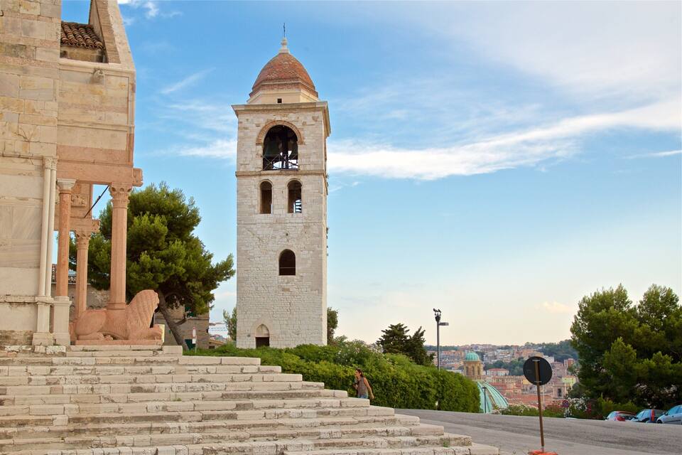 Uma torre de pedra com cúpula e janelas em arco, cercada por degraus e vegetação.